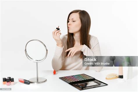 아름 다운 젊은 여 자가 그림을 흰색 배경에 고립 설정된 얼굴 장식 화장품으로 메이크업을 적용 하는 테이블에 앉아 빨간