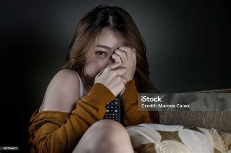 젊은 매력적이 고 귀여운 무서 워 아시아 한국 여자 보고 공포 영화 또는 Tv 드라마 지주 리모컨 두려움과 공황 얼굴 표현에 집 거실 소파에서 혼자 Brand Name