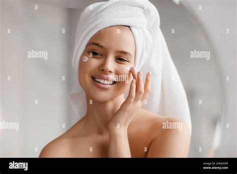 Headshot Of Woman Applying Facial Cream On Cheeks Smiling At Her