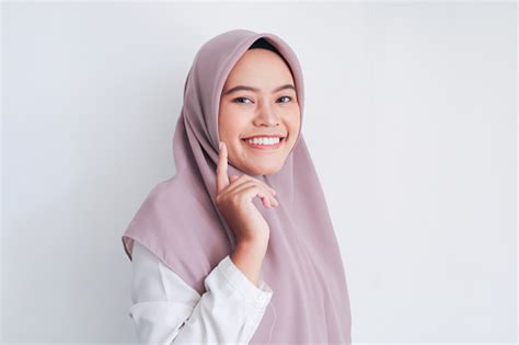 젊은 아시아 이슬람 여성은 미용 포즈에서 부드럽게 손가락으로 얼굴을 만지는 깨끗한 신선한 흰색 피부와 머리 스카프를 입고 인도네시아 여성 회색 배경에 고립 된 뷰티 컨셉