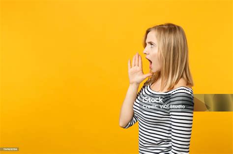 스튜디오에서 노란 주황색 벽 배경에 고립 된 입 근처의 손 제스처와 비명 줄무늬 옷에 젊은 여자의 측면 보기 사람들은 진심으로 감정 라이프 스타일 개념입니다 복사 공간을