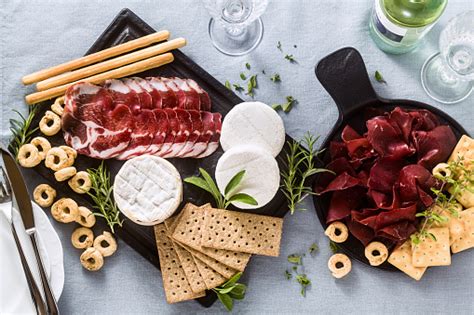 차가운 커트와 치즈는 파란 리넨 축제 식탁보에 향기로운 허브가 있는 화이트 와인 크래커 그리 시 니 및 타 갈리와 테이블의