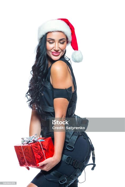 크리스마스 Ems 정장과 산타 클로스 모자를 쓴 젊은 운동 여성이 고립된 흰색 배경에 선물 상자를 들고 있습니다 Ems 교육 전기 근육 자극기 12월에 대한 스톡 사진 및