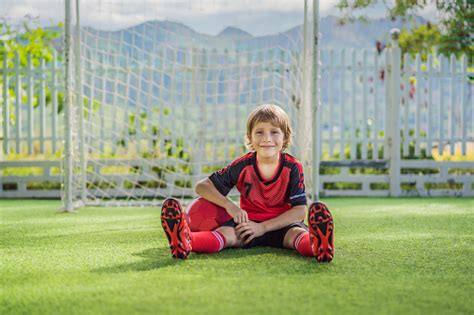 빨간 축구 유니폼을 입은 귀여운 소년이 야외에서 축구 축구를 하고 있다 아이들이나 아빠와 함께 스포츠를 하는 활동적인 아이 여름에 즐거운 미소를 짓는 행복한 소년 6 7