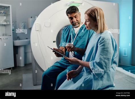 Biracial Radiographer Sitting On Ct Scanner Bed Showing X Ray Image To