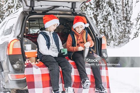크리스마스를 위해 장식 된 자동차 트렁크에 보온병이있는 빨간 산타 모자를 쓴 두 친구 십대 소년 도로 여행 모험과 지역 여행 개념 눈 덮인 숲에서 겨울 피크닉 새해 휴가