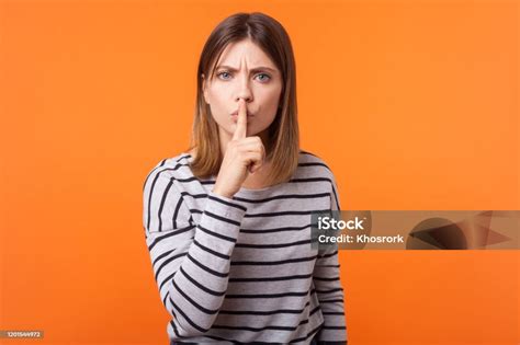 조용히 하세요 긴 소매 줄무늬 셔츠에 갈색 머리를 가진 심각한 여자의 초상화 오렌지 배경에 고립 된 실내 스튜디오 샷 20 29세에 대한 스톡 사진 및 기타 이미지 Istock