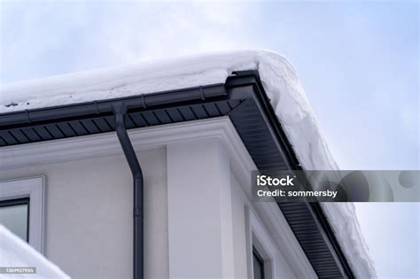 금속 다운 파이프 시스템 거터링 시스템 눈 아래 외부 하강 파이프 및 배수 파이프 회색 금속 타일로 만든 지붕과 겨울에 눈의 두꺼운 층으로 덮여 배수로와 집의 모서리