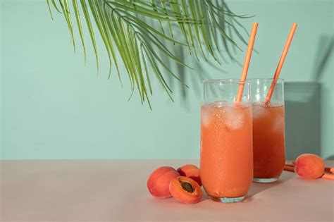 과일 살구가 담긴 두 잔 얼음과 빨대를 곁들인 칵테일 음료 복숭아 분홍색 테이블에 과일과 자른 과일 열대 야자수 잎 햇빛