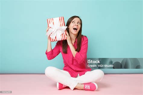 바닥에 앉아 장미 셔츠 블라우스 흰색 바지에 전체 길이의 초상화 여자 밝은 분홍색 파란색 파스텔 벽 배경 스튜디오에 고립 된 선물 상자를 개최 합니다 패션 라이프 스타일