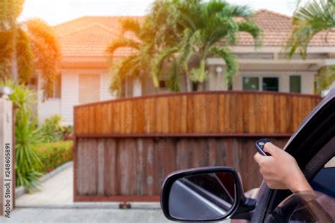 Woman In Car Hand Using Remote Control To Open The Automatic Gate With Modern Home Background