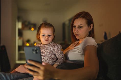 작은 백인 아이 어린 소녀 유아 어머니와 딸은 소파 침대에서 집에서 밤에 어두운 방에 앉아 휴대 전화로 만화 나 영화를보고있는 실제 사람들 가족이 카피 공간을 자라게합니다
