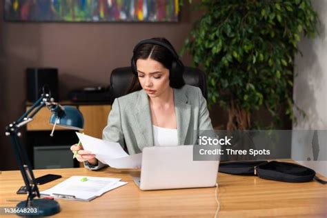 헤드폰을 낀 진지한 젊은 여성이 집에서 실내 테이블에 앉아 노트북과 종이로 고객과 화상 대화를 나눈 채 일하고 있다 교육에 대한 스톡 사진 및 기타 이미지 Istock