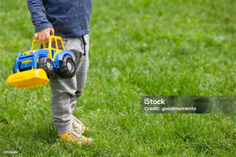 공원의 녹색 잔디에 서 있는 동안 다채로운 장난감 트랙터를 들고 유아의 손의 근접 촬영 아이는 보육 또는 유치원에서 차를가지고 노는 야외에서 산책 하는 아이 라이프 스타일