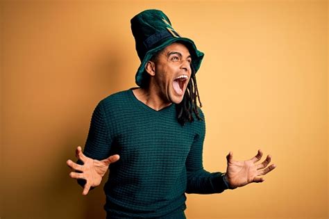 녹색 모자를 쓰고 있는 젊은 아프리카계 미국인 남성이 성패트릭의 날을 축하하는 클로버와 함께 미친 듯이 외치고 공격적인 표정과 팔을 들고 소리쳤다 좌절 개념입니다 St