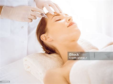 햇볕이 잘 드는 의료 센터에서 눈을 감고 미용 주사를 받는 아름다운 여성 미용사 의사는 주사기로 여성의 얼굴에 미용 시술을 하고 있다 미용 의학 및 수술 개념 20 24세에