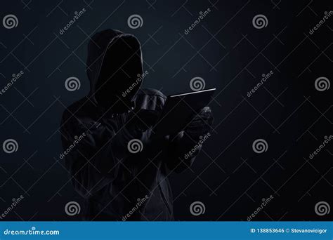 Hooded Computer Hacker With Obscured Face Using Digital Tablet Stock