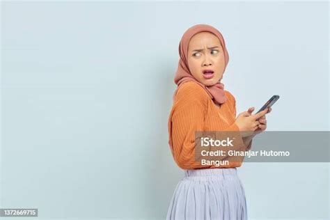 갈색 스웨터와 히잡에 놀란 젊은 아시아 무슬림 여성의 초상화 휴대 전화를 사용하고 흰색 배경에 고립 된 복사 공간을보고 무슬림 생활 방식 개념 25 29세에 대한 스톡 사진