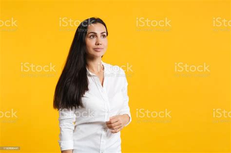 흰색 캐주얼 셔츠에 아름 다운 멋진 젊은 여자의 초상화는 스튜디오에서 밝은 노란색 오렌지 벽 배경에 고립 옆에 서 있는 사람들 라이프 스타일 개념입니다 복사 공간을 모의