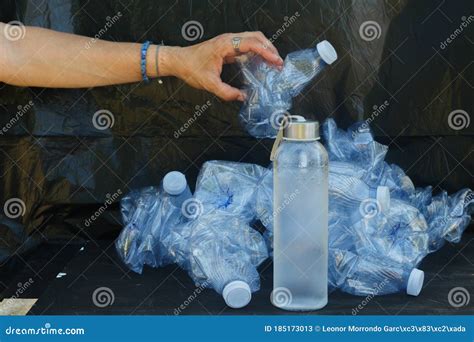 Hand With Glass Water Bottle In Front Of Stack Of Plastic Bottles