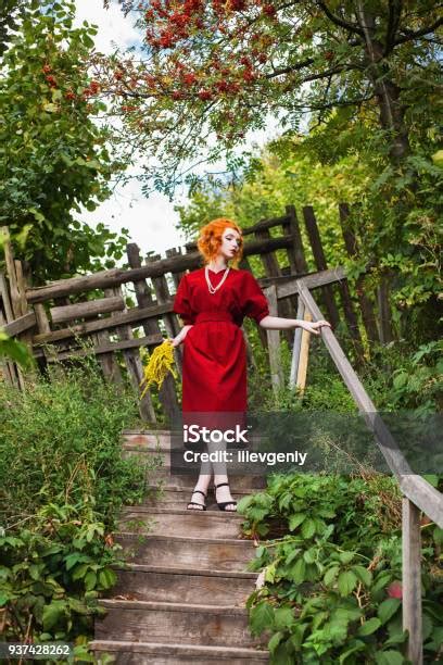 붉은 머리를 가진 여자와 컸 었 빨간색 노란색 꽃의 부케와 함께 손에 드레스 창백한 피부 파란 눈 및 그녀의 목 구슬의 목걸이와 밝은 특이 한 모양으로 빨간 머리 소녀