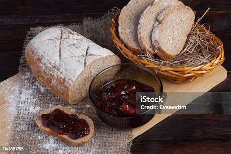 맛 있는 잼의 그릇 옆에 린 넨 패브릭과 나무 배경에 흩어진 밀가루가 있는 오크 보드의 고리 버들 그릇에 갓 슬라이스 한 조각 빵 0명에 대한 스톡 사진 및 기타 이미지