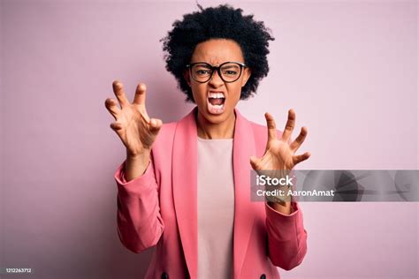 고양이 공격적이고 섹시한 표현으로 발톱 제스처를하고 재미 웃고 핑크 재킷을 입고 곱슬 머리를 가진 젊은 아름다운 아프리카 계