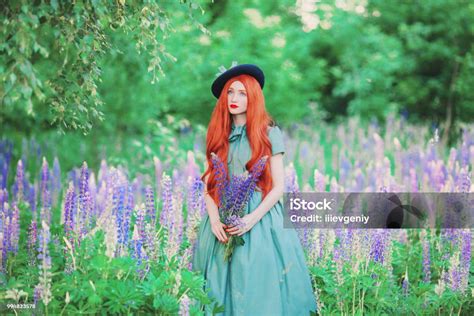 루피 너 스 배경에 매우 긴 머리를 가진 젊은 낭만적인 빨강 머리 소녀 민트에 멋진 르네상스 여자 드레스 아름 다운 꽃의 배경 루피 너 스 봄 풀밭에 성장 한다 낭만적인