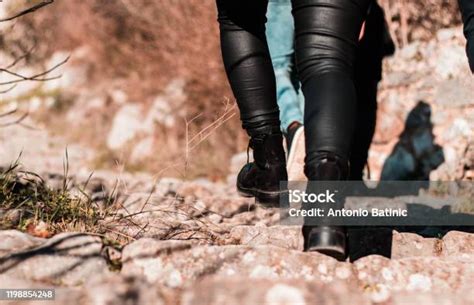 검은 색 바지와 검은 색 부츠의 다리가 돌 길을 하이킹합니다 배경에 오렌지 건조 잔디와 바위 포지엘지 보스니아 헤르체고비나의