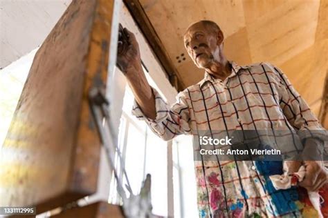 카메라 앞에 브러시가 서 있는 성숙한 또는 수석 회색 화가 스튜디오 나 집에서 일하는 페인트 스테인드 셔츠를 입은 진지한 남자 에센셜 오일에 대한 스톡 사진 및 기타 이미지