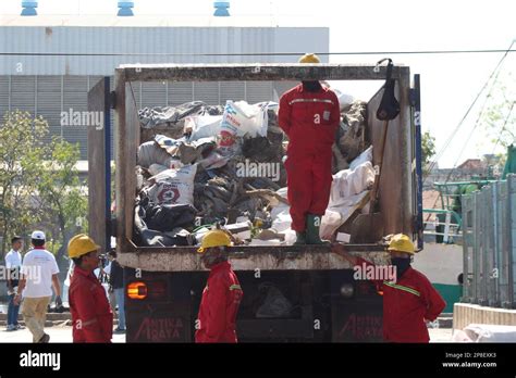 Cleaners In Uniform Are Collecting Garbage Into A Garbage Truck In The