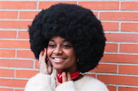 흰색 완벽한 미소 긴 아프로 머리와 벽돌 벽에 빨간 헤드폰으로 음악을 듣고 흰색 점퍼와 쾌활한 꿈꾸는 평온한 아프리카 계 미국인 여성의 측면 보기 초상화 20 29세에 대한