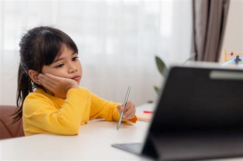 혼자 앉아서 지루한 얼굴로 밖을 내다보는 어린 아시아 소녀 숙제에 지루한 슬픈 지루함으로 테이블 위에 머리를 얹은 미취학 아동 버릇없는 아이 4 5세에 대한 스톡 사진 및