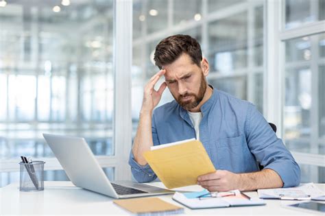 파산에 대한 나쁜 소식 메일 메시지 사무실 안에서 화가 난 남자는 편지가 든 봉투를 들고 알림을 읽고는 실망했습니다 직장에서 사무실 내부의 불만족스러운 근로자 35 39세에