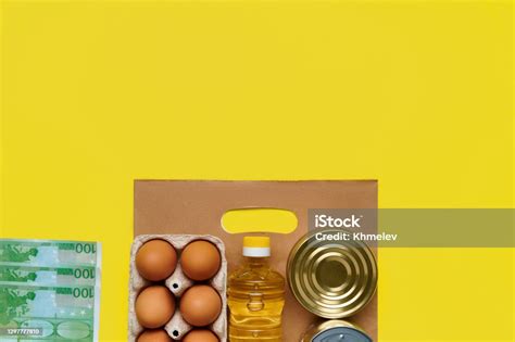 노란 배경에 종이 봉투가있는 계란 통조림 음식 해바라기 기름 및 돈 유로 지폐 공간 평평한 평지 복사 코로나바이러스 검역 격리 기간의 위기 식품 음식 배달 기부 0명에 대한