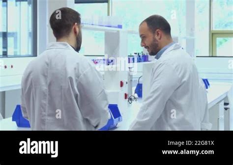 Two Male Scientists In White Lab Coats Discuss A Research Project