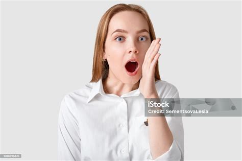 놀란된 여자의 사진 크게 놀람 열린된 입 근처 팜 흰 셔츠 포즈 스튜디오 벽에 옷을 입고 가장 친한 친구와 때로 사람들 얼굴 표정 그리고 반응 개념 곁눈질에 대한 스톡 사진