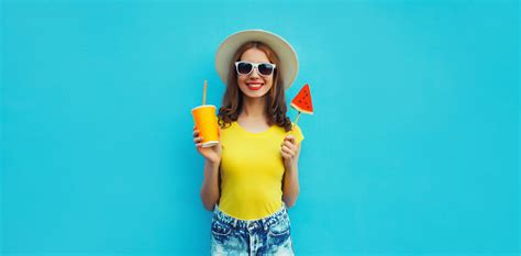 파란색 바탕에 밀짚모자를 쓰고 막대 사탕이나 아이스크림 모양의 수박 조각으로 주스를 마시는 행복한 미소 짓는 젊은 여성의 여름 초상화 25 29세에 대한 스톡 사진 및 기타