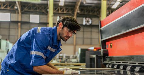 백인 잘 생긴 남성 산업 노동자는 제조 공장에서 일합니다 매력적인 청년 산업 공장 엔지니어가 헬멧을 착용하고 제조 공장에서 주문 및 제품을 행복하게 처리합니다 사진