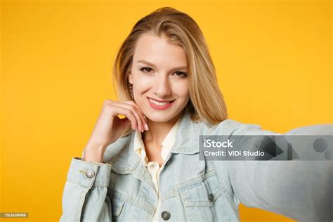 가까이에서 매력적인 아름 다운 젊은 여자의 셀 카 샷 데님 캐주얼 옷 스튜디오에서 노란색 주황색 배경에 고립 된 턱에 손을 넣어 사람들 라이프 스타일 개념입니다 복사 공간을