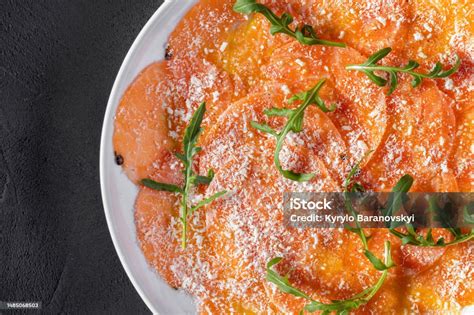 파마산 치즈와 루꼴라를 곁들인 연어 카르파초 Carpaccio는 흰색의 둥근 세라믹 접시 위에 놓여 있습니다 접시는 회색 돌 배경에 서 있습니다 건강한 생활방식에 대한 스톡