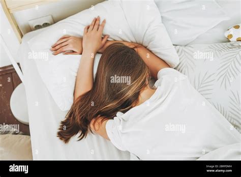 Young Woman With Long Dark Hair Sleeping In Bed With White Linen At