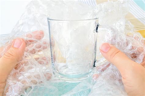 여자 손 흰색 파란색 체크 무늬 식탁보에 투명 거품 랩 클래식 유리 차 컵을 포장 안전한 운송을 위해 깨지기 쉬운 물품을 포장하기위한 재료 가정 생활에 대한 스톡 사진 및