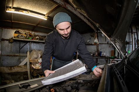 차고에서 자동차의 더러운 공기 필터를 교체하는 청년 그는 한 손에 에어 필터를 들고 다른 손은 자동차 후드에 무언가를 조이고