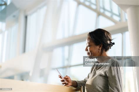 사무실 건물 복도에서 휴대 전화를 사용하는 웃는 아프리카 계 미국인 사업가 Brand Name Online Messaging Platform에 대한 스톡 사진 및 기타