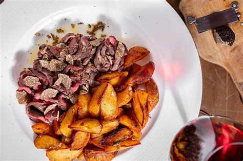 강판 트러플과 튀긴 감자를 곁들인 얇게 썬 고기와 와인 한 잔과 메인 코스가 테이블 위에 놓여 있습니다 감자 요리에 대한 스톡 사진 및 기타 이미지 Istock