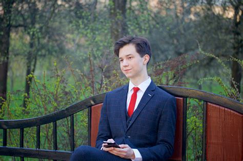 젊은 사람 십 대 클래식 정장 봄 공원에서 빈티지 벤치에 앉아 있다 그는 그의 손에 스마트폰을 보유 하 고 거리에 신중 하 게 보인다 긍정적인 감정 표현에 대한 스톡 사진