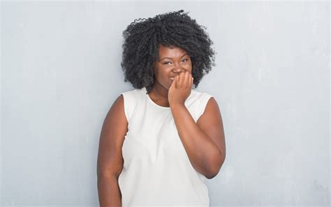 강조 하 고 손톱을 물어 뜯고 입에 손을 긴장을 찾고 회색 그런 지 벽에 젊은 아프리카계 미국인 여자 불안 문제입니다 감정에