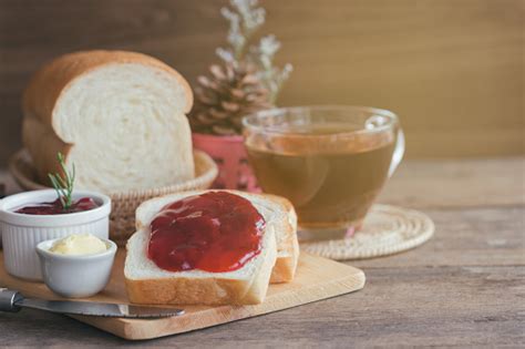 맛 있는 토스트 버터와 빵 그리고 소박한 나무 테이블 복사 공간에 넣어 나무 절단 보드에 뜨거운 차를 곁들인 딸기 잼을 가진 퍼짐 수 제 베이커리 개념입니다 아메리칸 조식
