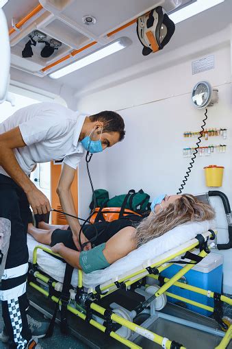환자를 돕는 얼굴 마스크를 가진 남성 구급대원은 전염병 도중 구급차에 있는 환자의 혈압을 측정합니다 구급차에 대한 스톡 사진 및